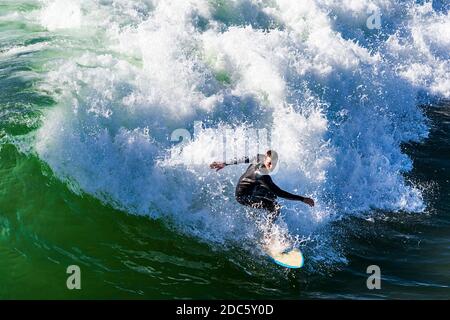 A surfer rides a wave as a king tide hits Huntington Beach, California ...