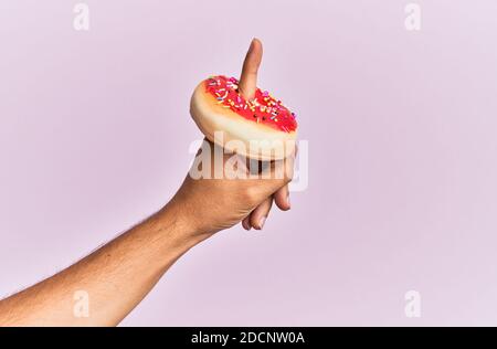 Finger of hispanic man holding donut over isolated pink background ...