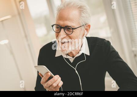 Senior businessman using earphones during conversation on mobile phone ...