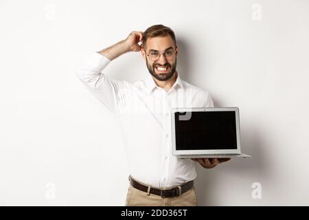 Awkward business man showing laptop screen and looking doubtful ...