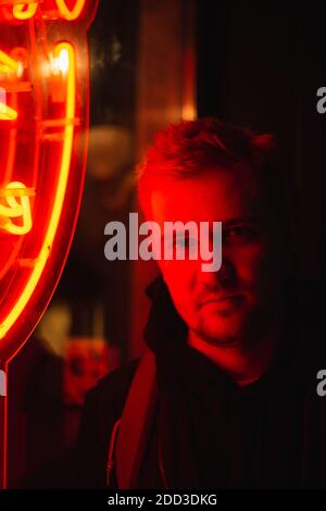 Portrait of a hipster guy with colorful neon light on green studio ...