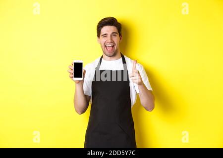 Happy waiter showing mobile screen and thumb up, recommending cafe ...