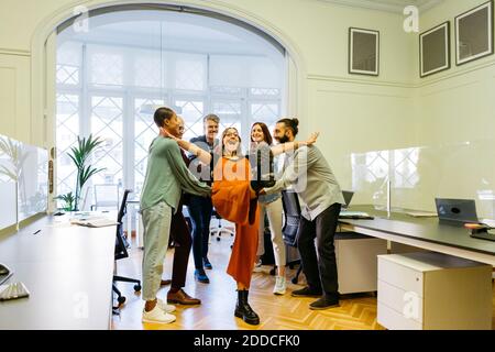 Cheerful businesswoman falling while coworkers catching at workplace ...