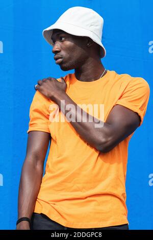 young man with cap and blue shirt is standing in front of mountain lake ...