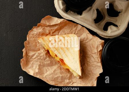 Toasted sandwich in craft paper with cup of coffee on table Stock Photo ...
