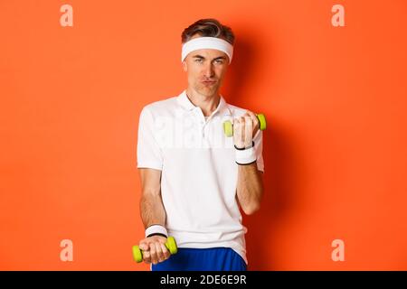 Portrait of cheeky middle-aged fitness guy, doing sports against orange ...