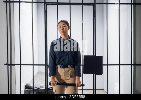 A young prison guard poses in front of prison bars in uniform. In a ...