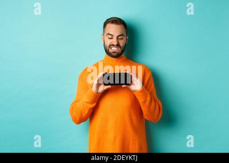 Image of man cringe at something on mobile screen, staring disgusted at ...