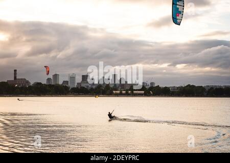 A woman kiteboarding on a summer evening with a dark Boston skyline ...