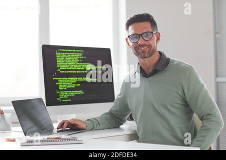 Portrait of mature computer programmer smiling at camera while working at the table with ...