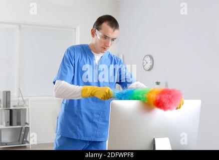 Male janitor cleaning computer in office Stock Photo - Alamy