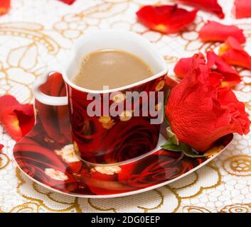 Little red roses in a cup, petals and jute rope on the wooden table ...