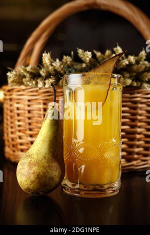 A glass of pear juice with ice and cut ripe fruits nearby on a gray ...