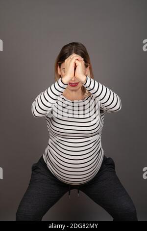 Pregnant woman preparing for labor, doing squats in front of grey ...