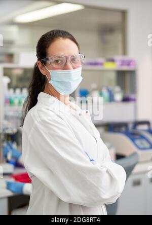 Scientist in goggles looking at camera near test tubes and microscope ...
