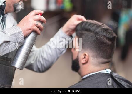 Master barber making modern hairstyle fixating hair with spray Stock ...