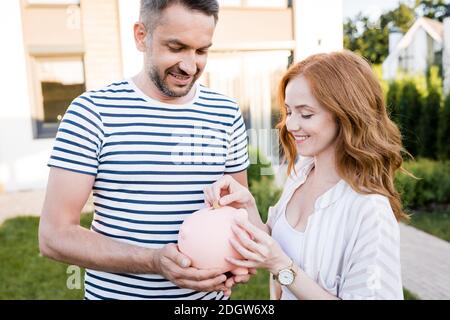 Caucasian woman putting money in a piggybank against a white background ...