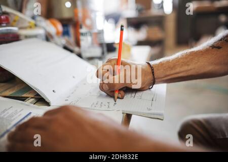 cropped view of carpenter writing in notebook while working in workshop ...