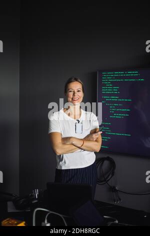 Portrait of mature computer programmer smiling at camera while working at the table with ...