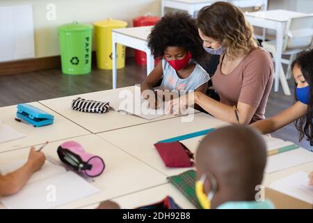 Female teacher wearing face mask holding digital tablet teaching to ...