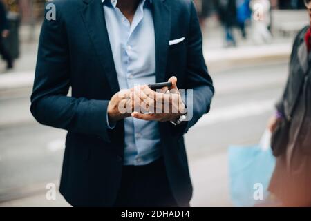 Midsection of mature businessman using smart phone while standing by ...