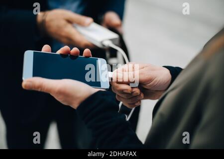 Midsection of businesswoman charging mobile phone while standing with ...