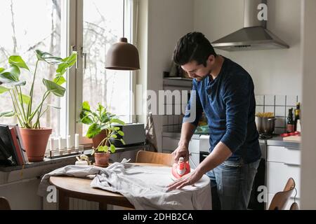 Young hispanic man ironing holding burned iron shirt at laundry room ...