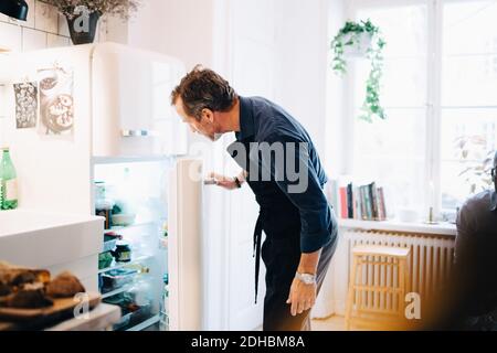 Adult man standing at refrigerator, choosing frozen convenience food in ...