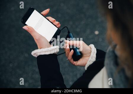 Midsection of mature businesswoman charging mobile phone while standing ...