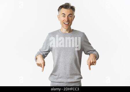 Handsome man pointing down with impressed and happy face, smiling and ...