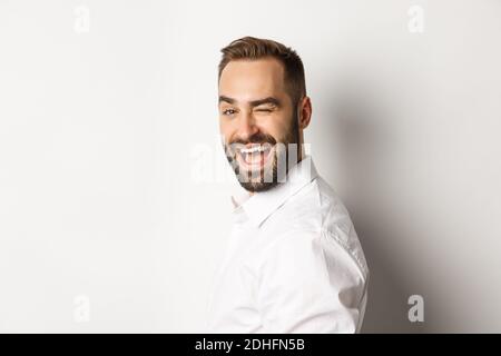 Close-up of cheeky guy with beard, turn face at camera and winking with ...