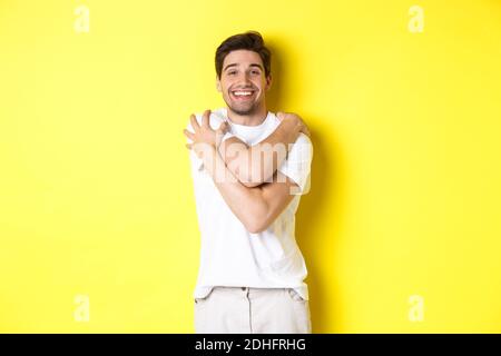Happy kind guy hugging himself and smiling, standing pleased against ...