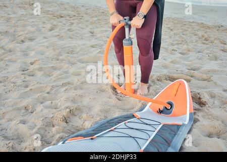 man in wetsuit inflating paddle board at the seashore on sandy beach ...