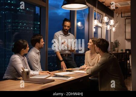 Multiracial colleagues work late at night in an office, discussing ...