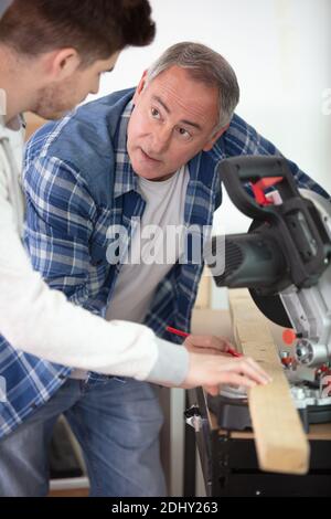 carpenter with apprentice cutting wood in workshop Stock Photo - Alamy