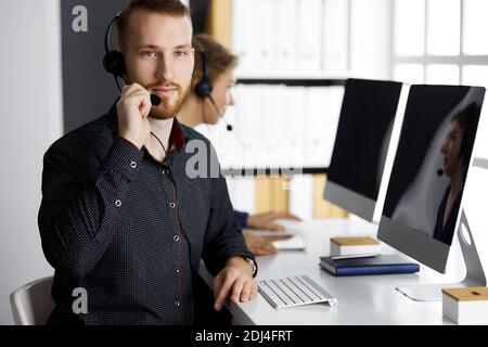 Red-bearded businessman talking by headset near his female colleague ...