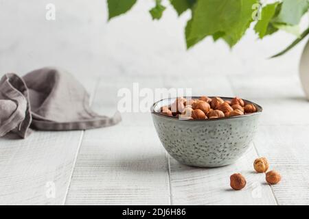 A handful of hazelnuts in a grey bowl on a white wooden background ...