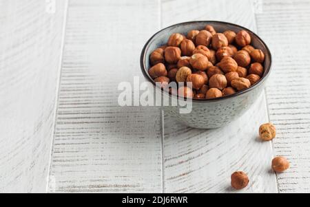 A handful of hazelnuts in a grey bowl on a white wooden background ...