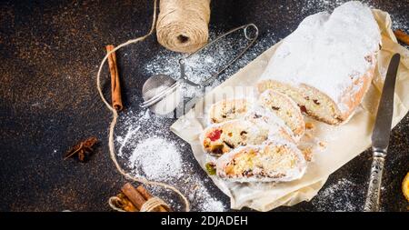 Stollen sliced on kraft paper on dark wooden table with xmas tree ...
