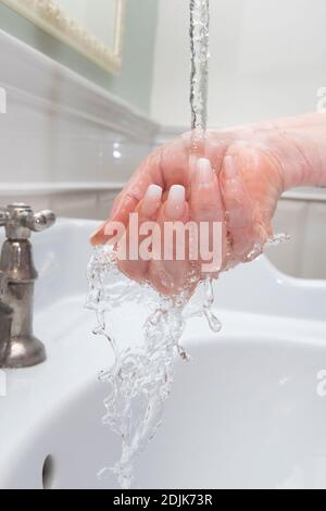 Woman washing hands under running water. A modern glass faucet from ...