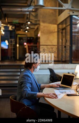 Cautious gentleman in face mask working on his laptop Stock Photo - Alamy