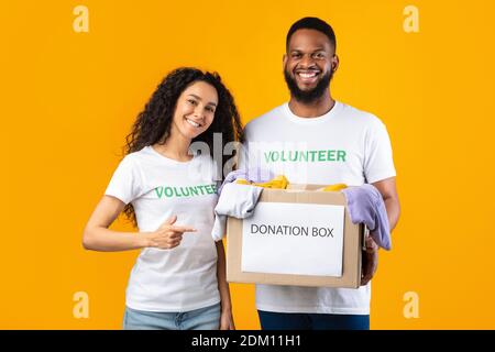 Two Cheerful Volunteers Holding Donation Box On Yellow Studio ...