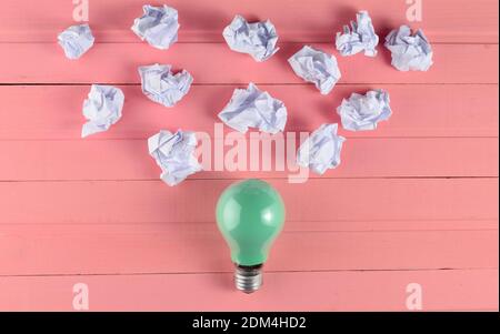 Incandescent bulb and crumpled white paper balls on brown wooden table ...