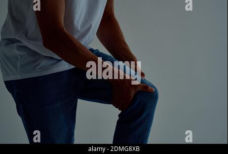 the guy touches his leg with his hands on a light background knee pain ...