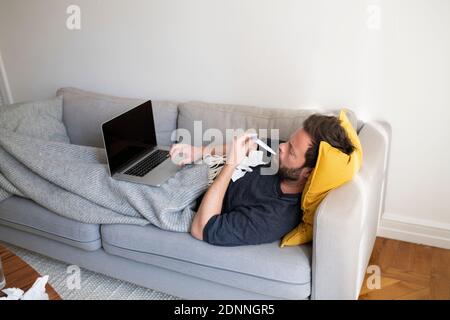 Man on sofa checking temperature Stock Photo - Alamy