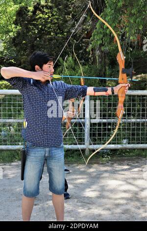 teenage boy holding archery bow pointed at the camera in portrait ...