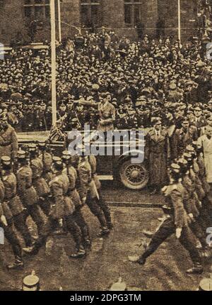 Adolf Hitler waving to crowds from his car at the head of a parade. The ...