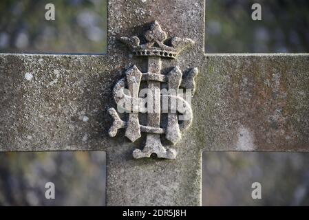 Old stone cross with IHS encryption against green foliage in St ...