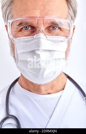Portrait of senior bearded doctor in white coat and face mask looking ...
