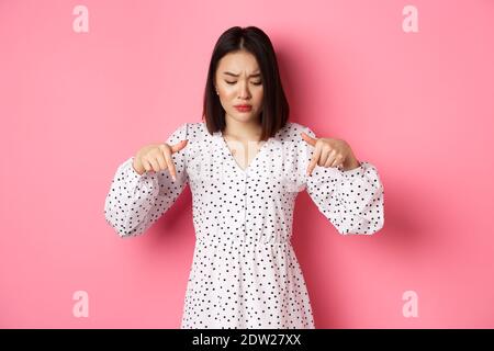 Concerned asian woman peeking down and pointing hand at disturbing ...